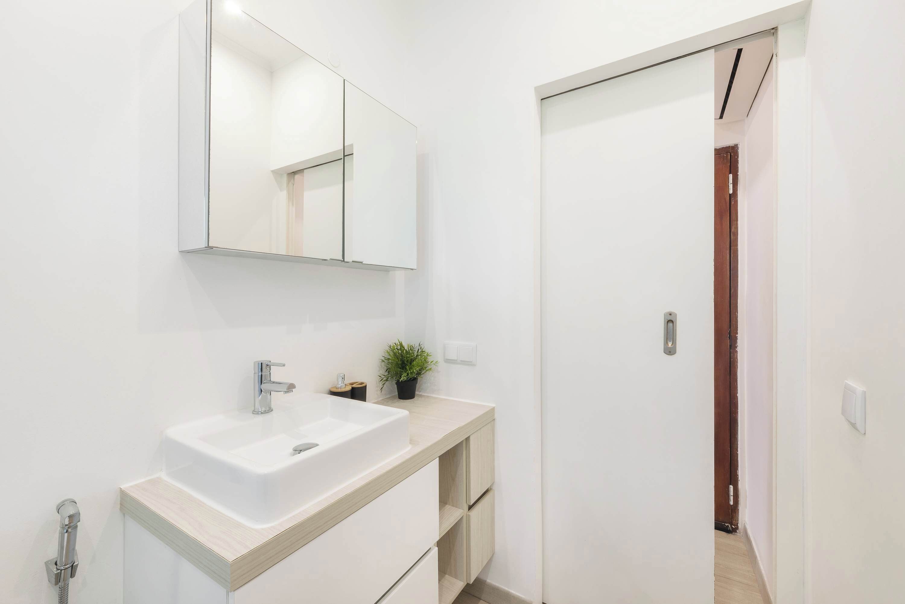 Casa de banho moderna com lavatório branco, espelho e toucador de madeira.