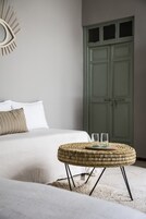 Um quarto com cama, um banquinho de fibra natural, um espelho e um guarda-roupa verde.