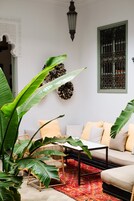 Quarto com sofá, cadeiras, mesa e grandes plantas verdes.