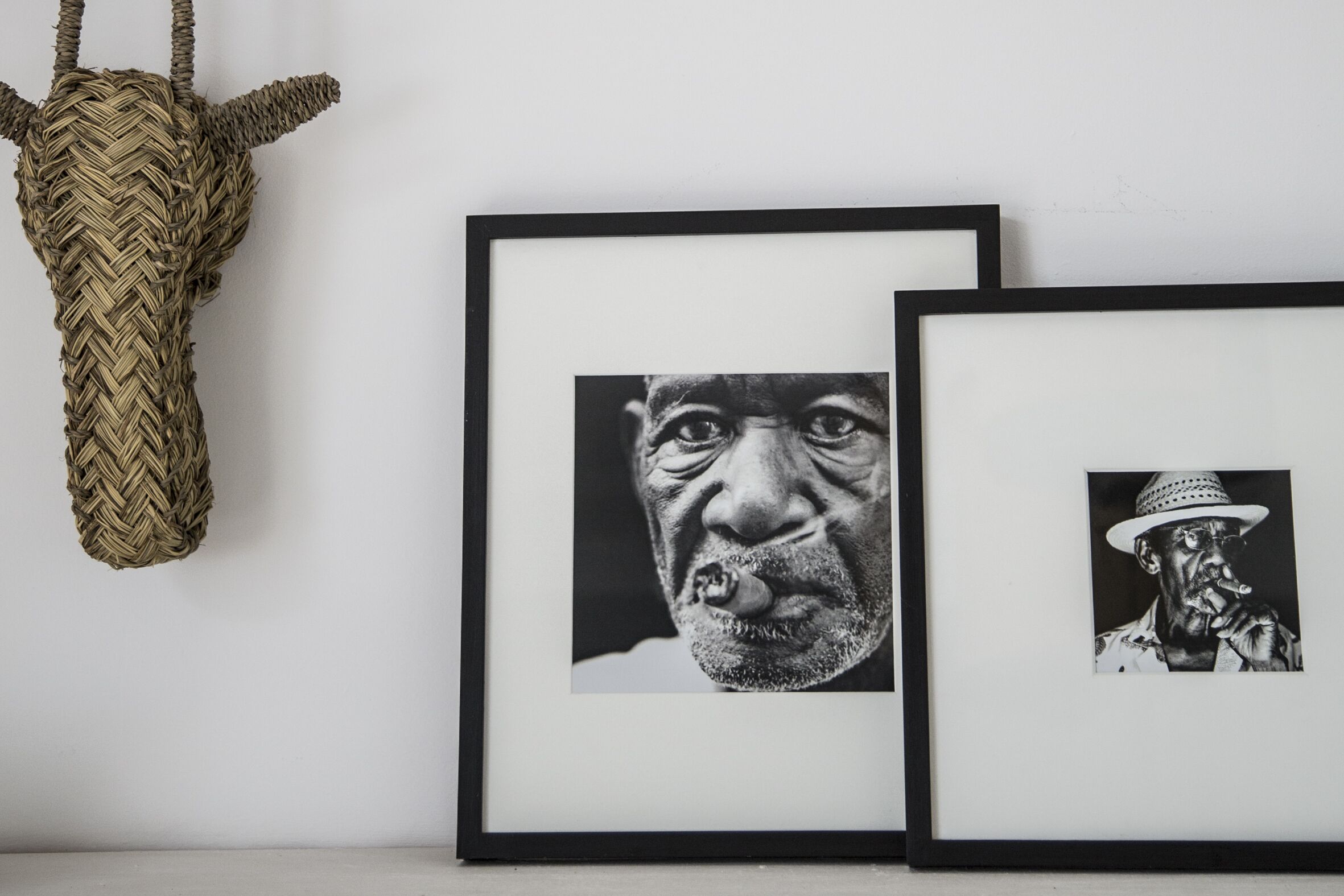 Um retrato emoldurado de um homem com chapéu, uma escultura de cabeça de animal em tecido e uma fotografia emoldurada numa parede.