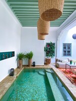 Uma área de piscina com piso ladrilhado, um sofá e cestos de vime suspensos.