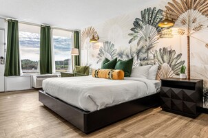 Quarto moderno com uma cama grande, cortinas verdes, um mural na parede e uma mesa de cabeceira.