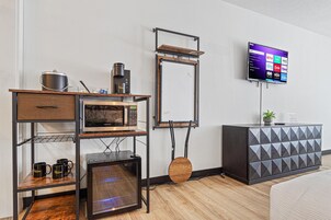 Quarto de hotel moderno com cozinha compacta, televisão de tela plana na parede e cama com edredom branco.
