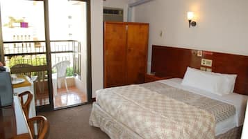 Quarto de hotel com cama, escrivaninha, cadeira, guarda-roupa e varanda com cadeira.