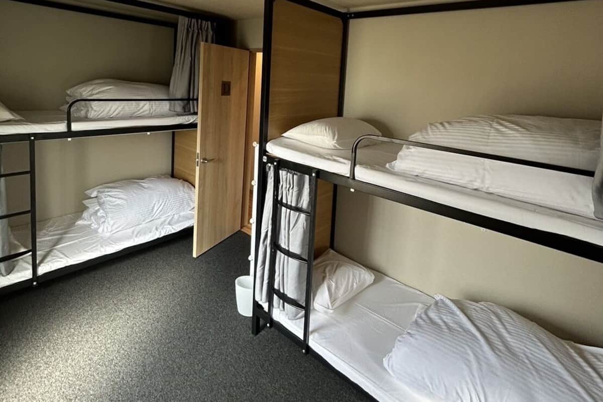 Quarto com beliche de três andares, guarda-roupa de madeira e uma pequena lixeira.