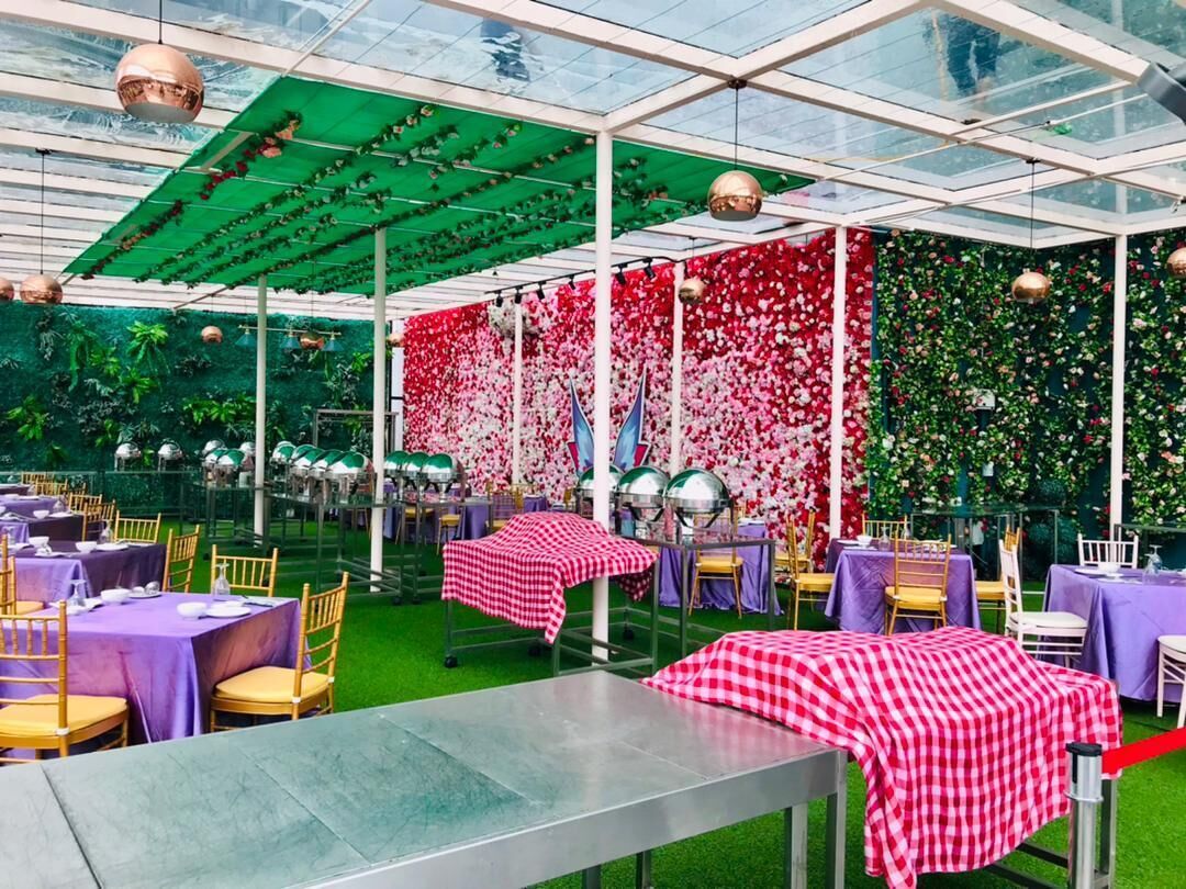 Um espaço para eventos interno com mesas, cadeiras, teto de vidro e arranjos florais decorativos.