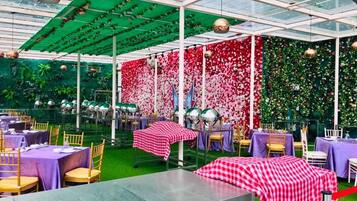 Um espaço para eventos interno com mesas, cadeiras, teto de vidro e arranjos florais decorativos.