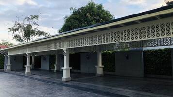 Uma área externa coberta com estrutura de telhado treliçada, colunas e luminárias fixadas na parede.
