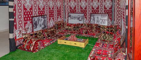 Quarto com carpete vermelho e branco estampado, piso de grama sintética verde e um baú de madeira no centro.