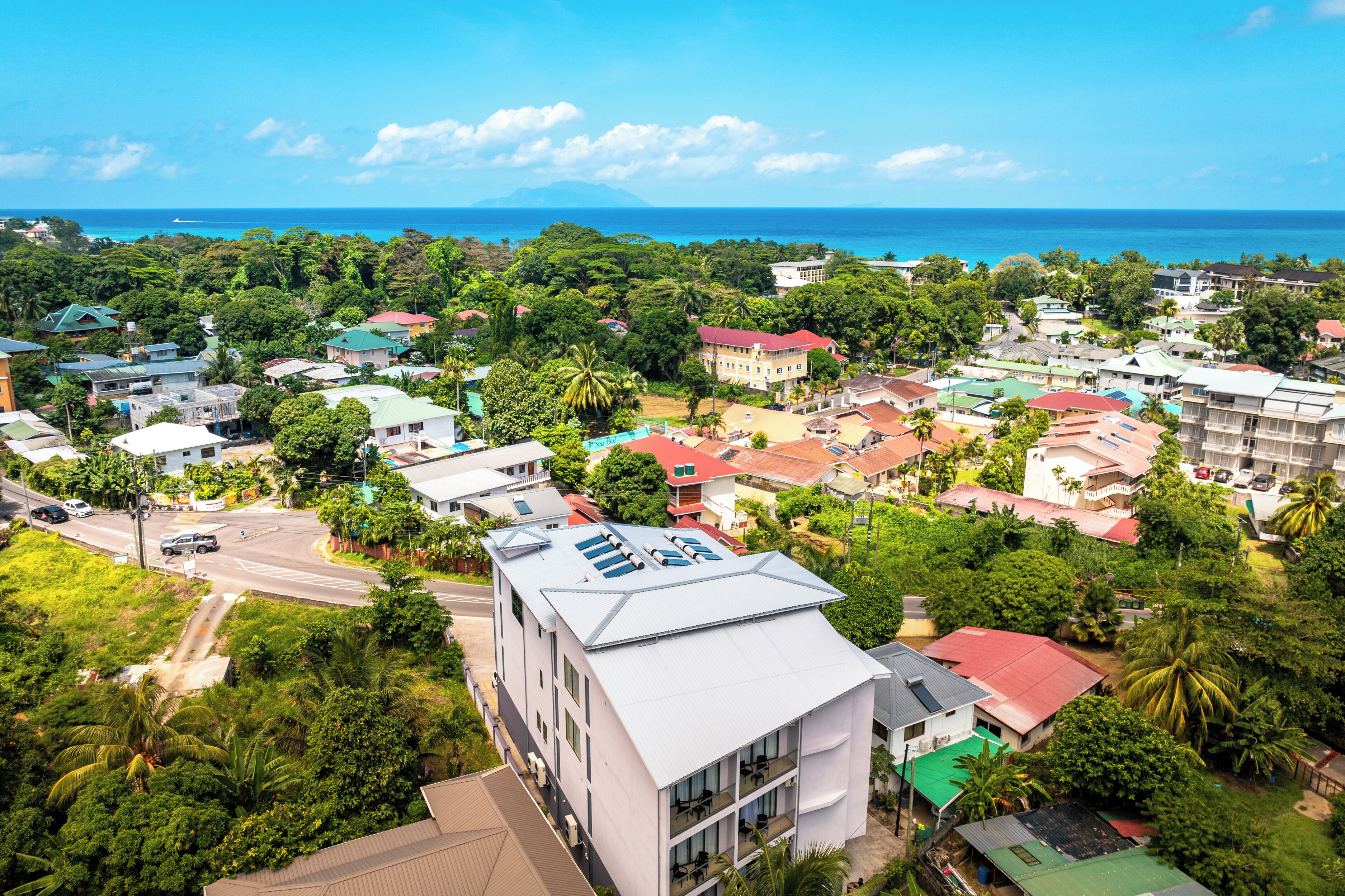 Uma cidade costeira com mistura de edifícios residenciais e comerciais, um edifício branco de destaque com telhado plano, e vista para o oceano.