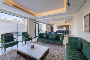 Um hall de hotel moderno com um conjunto de sofá verde, uma mesa de centro de mármore e uma área de refeições com cadeiras azuis.