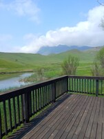 Um deck de madeira com vista para um lago e colinas ondulantes.