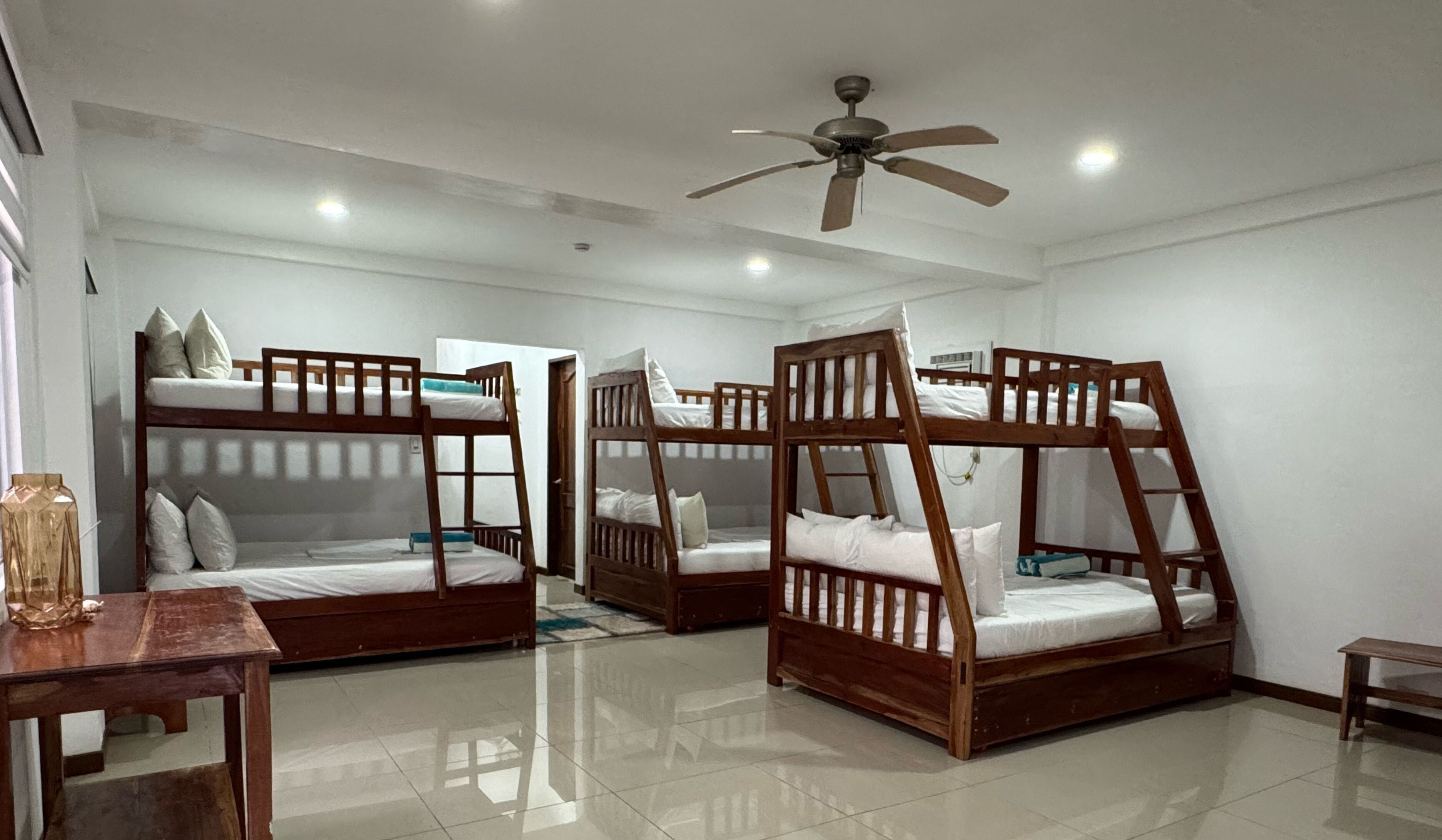 Um quarto com três beliches, um ventilador de teto e uma mesa pequena.
