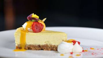 Uma fatia de cheesecake com um fio de caramelo dourado, coberta com uma morango, um pouco de creme e uma folha decorativa.