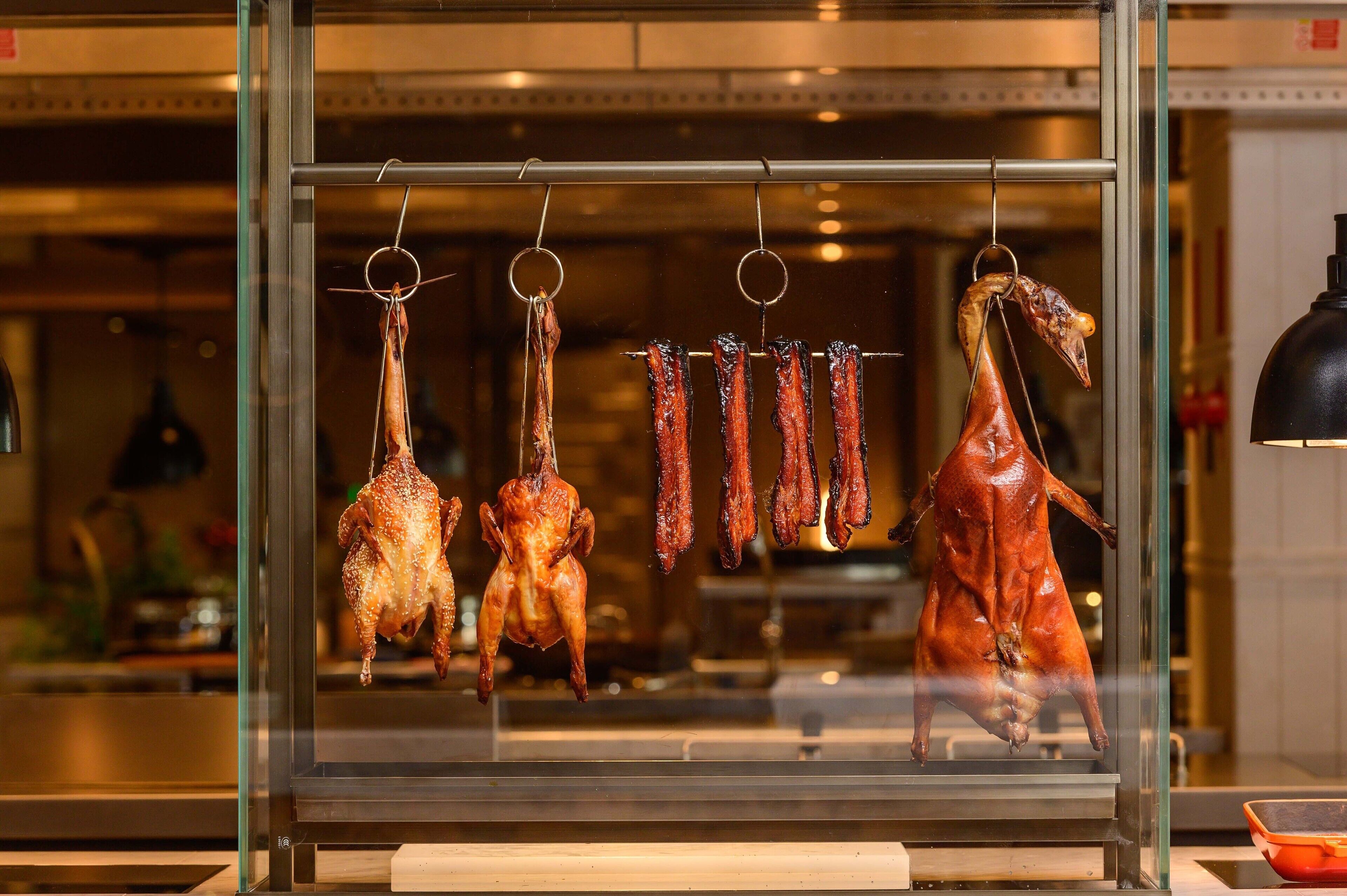 Diversos tipos de carne pendurados em uma vitrine, provavelmente em um restaurante ou empório.