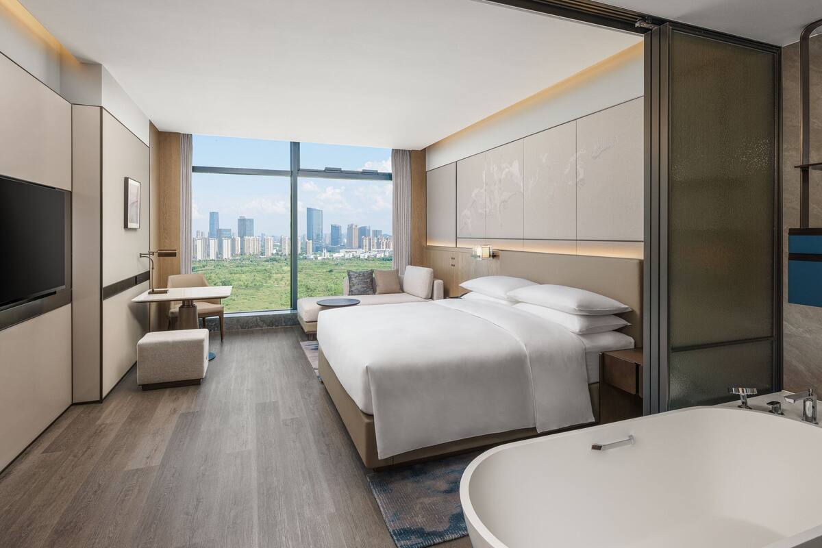 Quarto de hotel moderno com uma cama grande, área de estar, televisão e banheira.