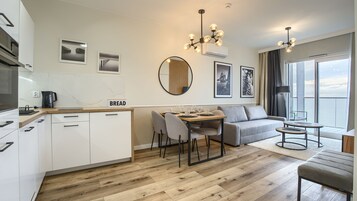 Cozinha moderna com cafeteira, mesa de jantar posta para quatro e um sofá numa sala de estar com vista.