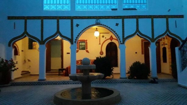 Um pátio com uma fonte, arcos e piso de azulejos.