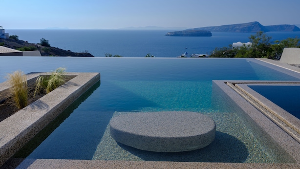 Uma piscina infinita azul cristalina com um elemento circular de pedra no centro, rodeada por uma área ajardinada com plantas.