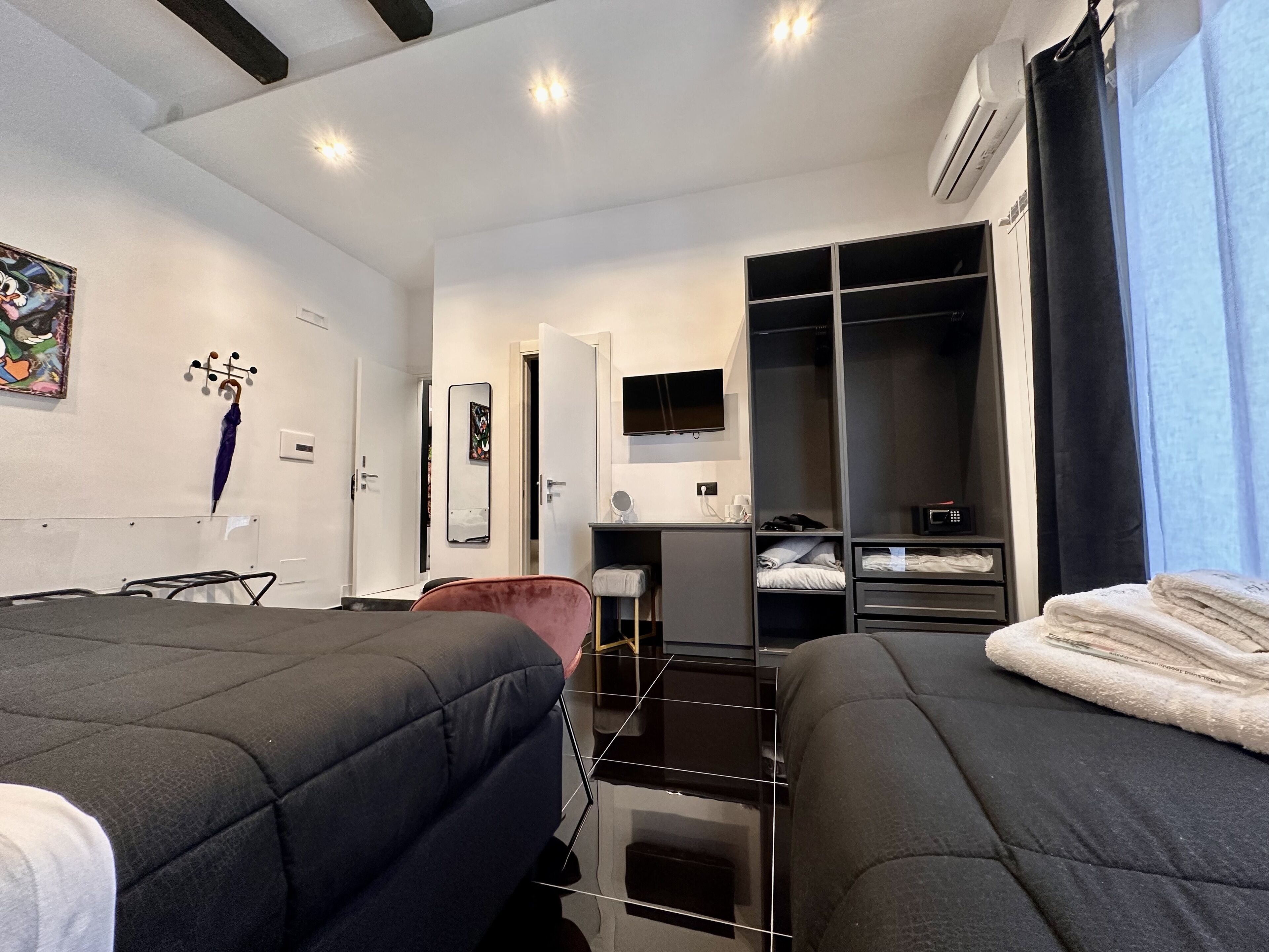 Quarto de hotel moderno com duas camas, uma escrivaninha, um guarda-roupa e uma televisão.