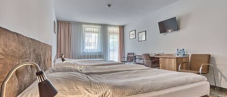 Quarto de hotel com duas camas, uma escrivaninha, uma cadeira, uma televisão e uma janela com cortinas.