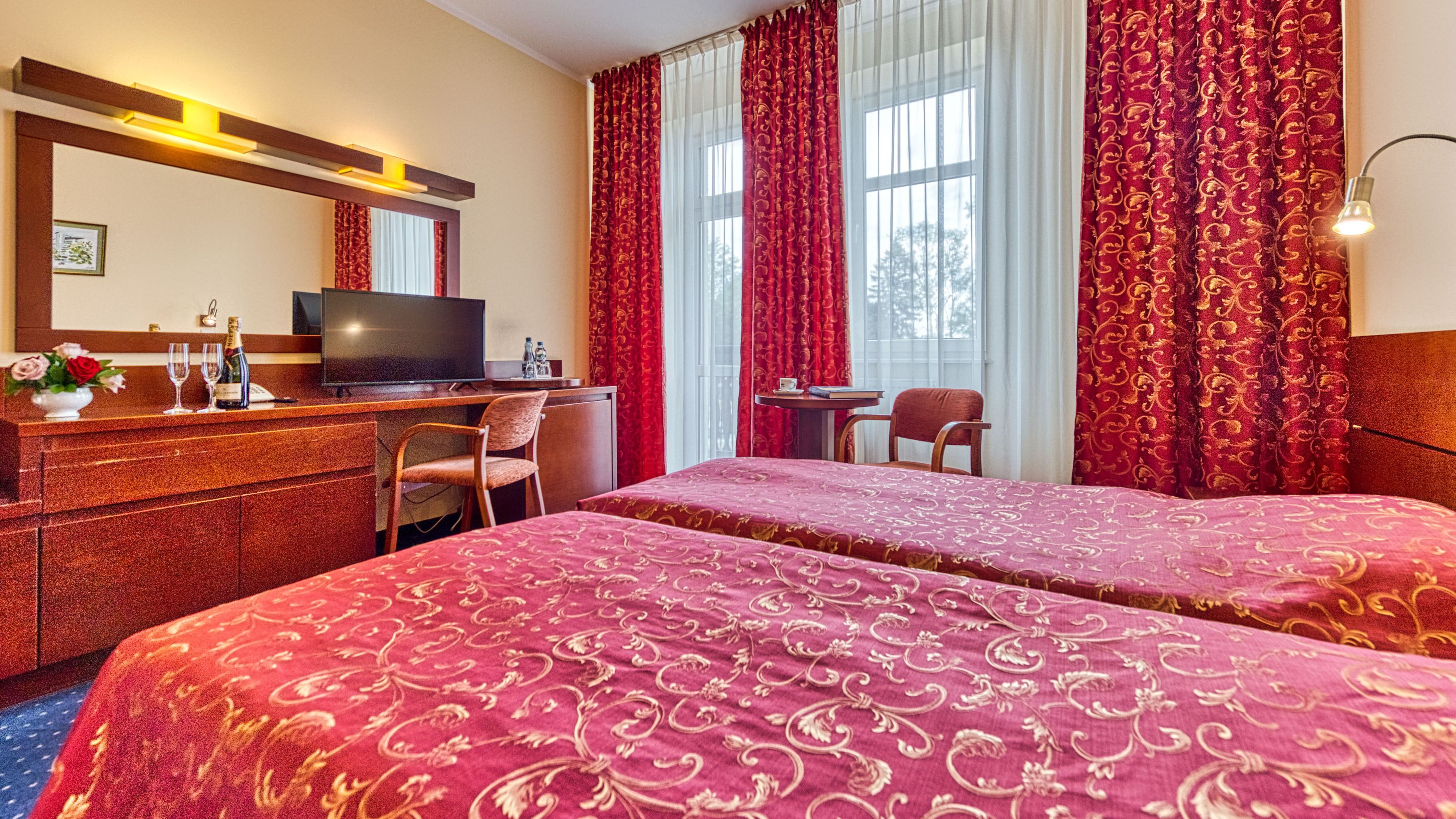 Quarto de hotel com uma cama grande, uma escrivaninha com televisão, uma cadeira e uma pequena mesa.