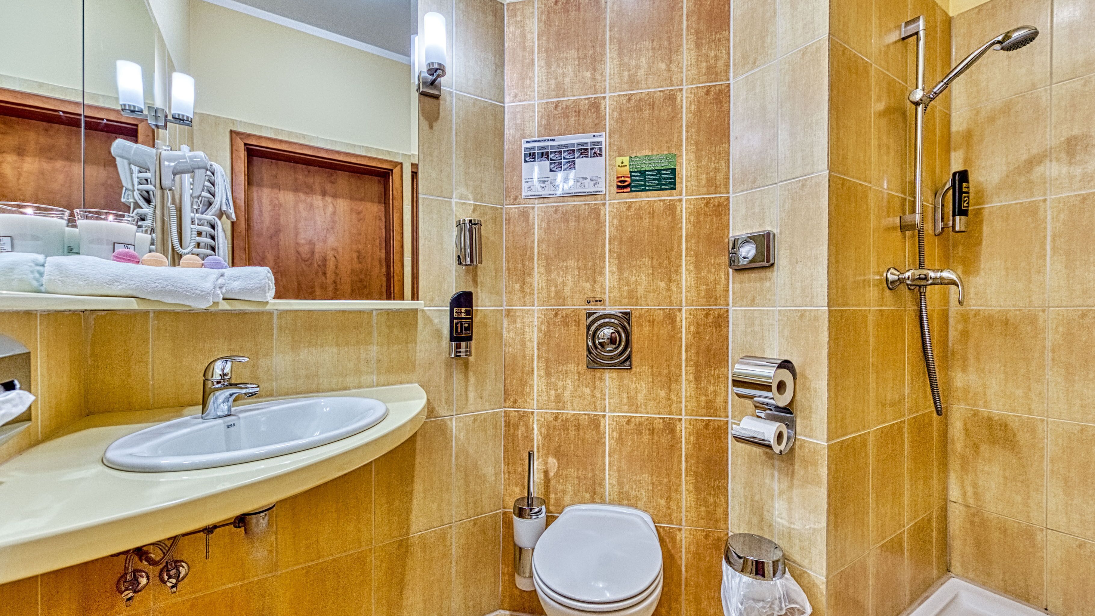 Casa de banho com lavatório, sanita e chuveiro. Há toalhas e um dispensador de sabonete no balcão do lavatório.