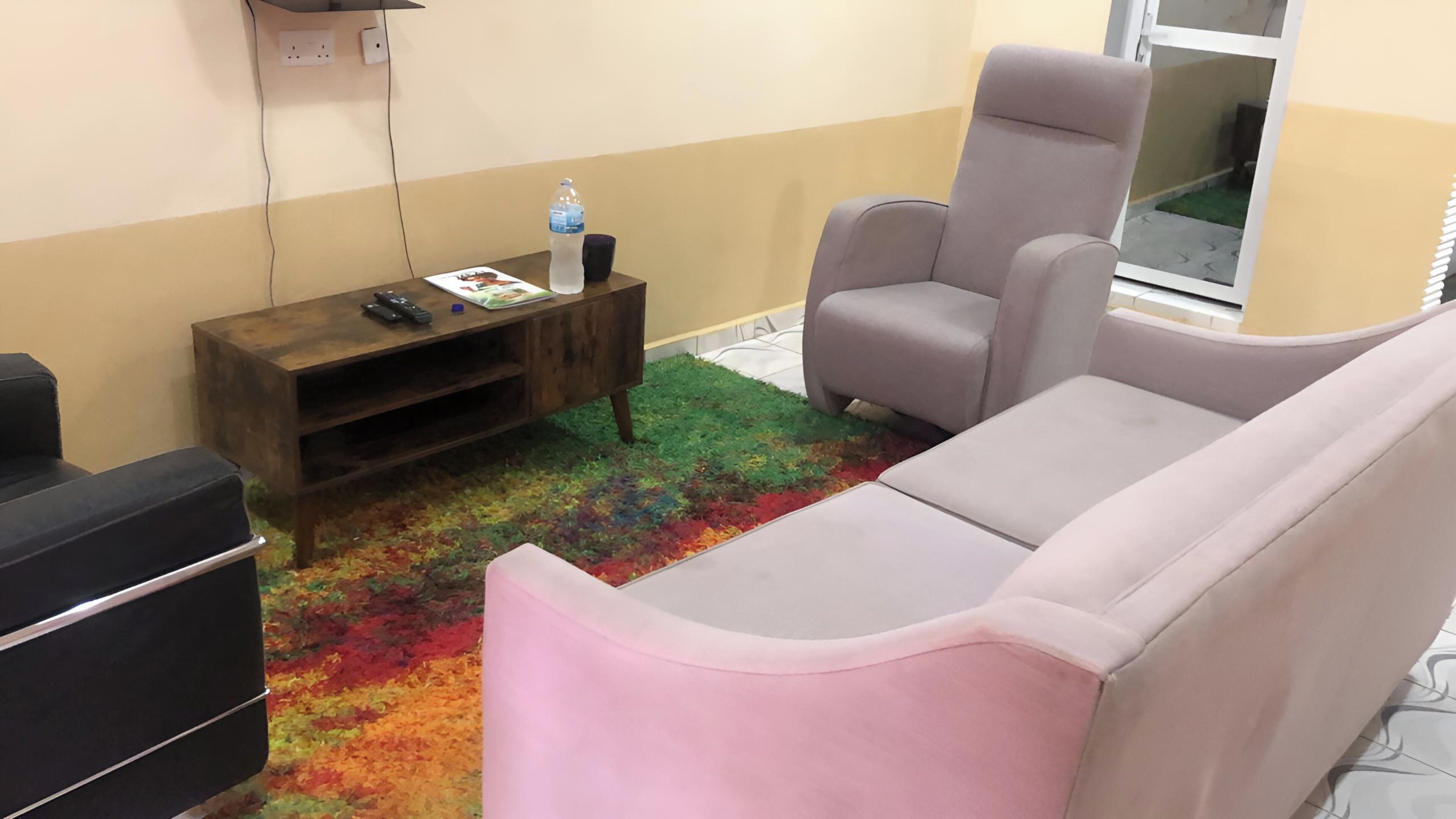 Quarto com um sofá rosa, uma poltrona cinza, uma mesa de centro de madeira e um tapete colorido.