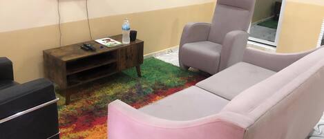 Quarto com um sofá rosa, uma poltrona cinza, uma mesa de centro de madeira e um tapete colorido.