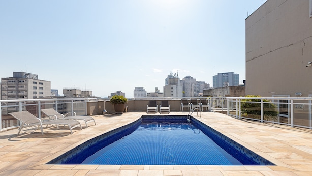 Piscina no terraço com espreguiçadeiras e um horizonte urbano ao fundo.