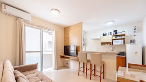 Uma sala de estar moderna com sofá, área de jantar com cadeiras, cozinha com micro-ondas e televisão.