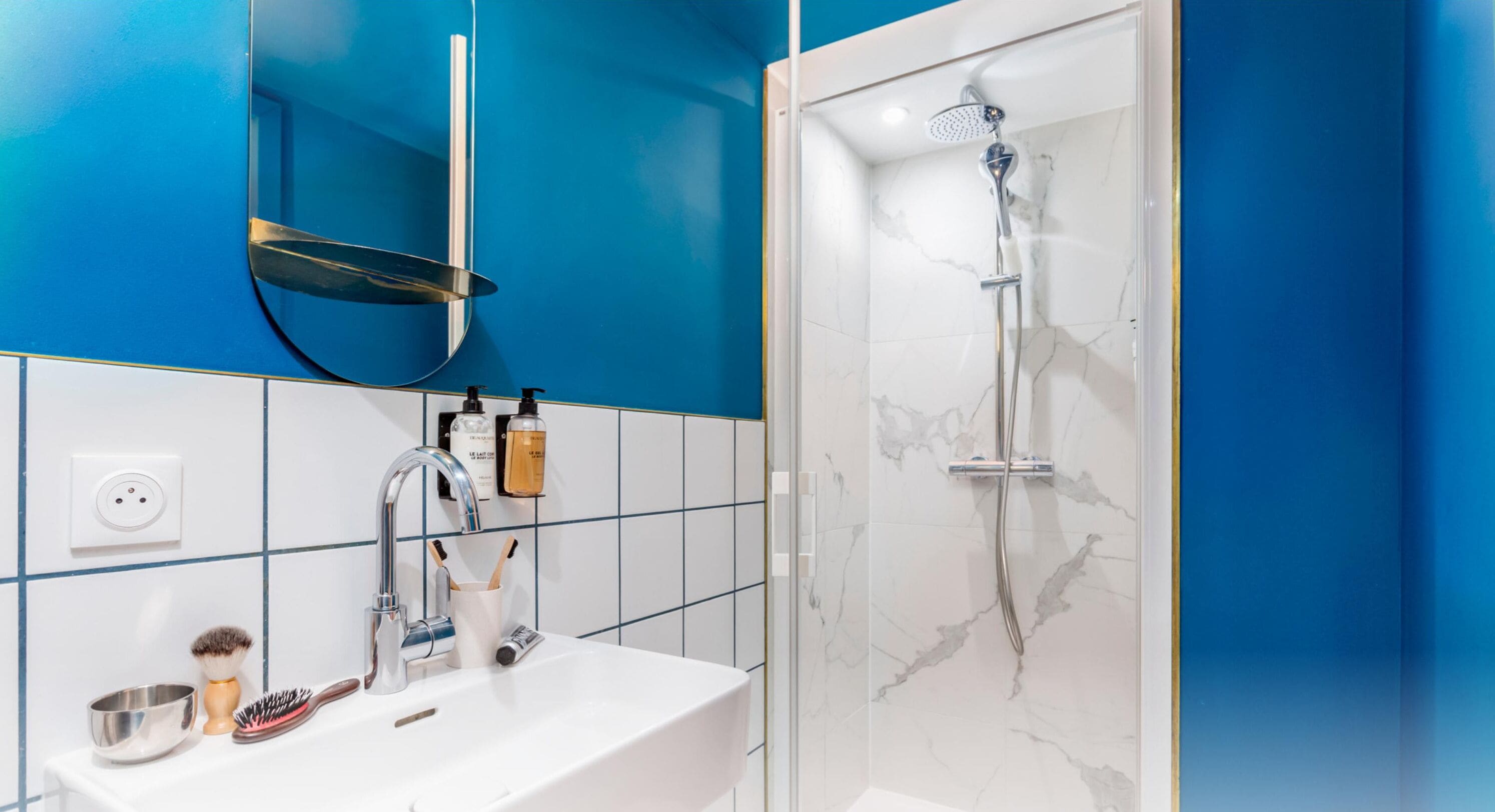 Casa de banho com uma pia branca, espelho, chuveiro com chuveiro manual e paredes revestidas de azulejos azuis.