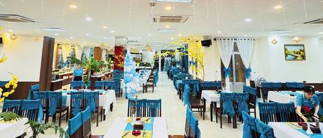 Um restaurante amplo com cadeiras e mesas azuis, decorado com balões e luzes de Natal.