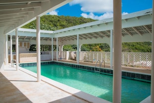 Piscina coberta com água cristalina, cercada por colunas brancas e um muro branco.