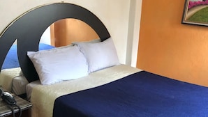 Quarto de hotel com cama, mesa de cabeceira com telefone e um quadro na parede.
