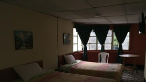 Quarto com duas camas, uma cadeira, uma mesinha e uma janela com cortinas.
