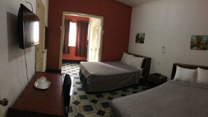 Quarto de hotel com duas camas, uma escrivaninha, uma televisão e piso ladrilhado.
