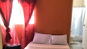 Uma cama de solteiro em quarto com paredes laranja, cabeceira de madeira e mesa de cabeceira com telefone.