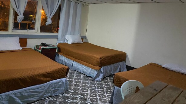 Quarto com duas camas, uma mesinha e janela com cortinas.