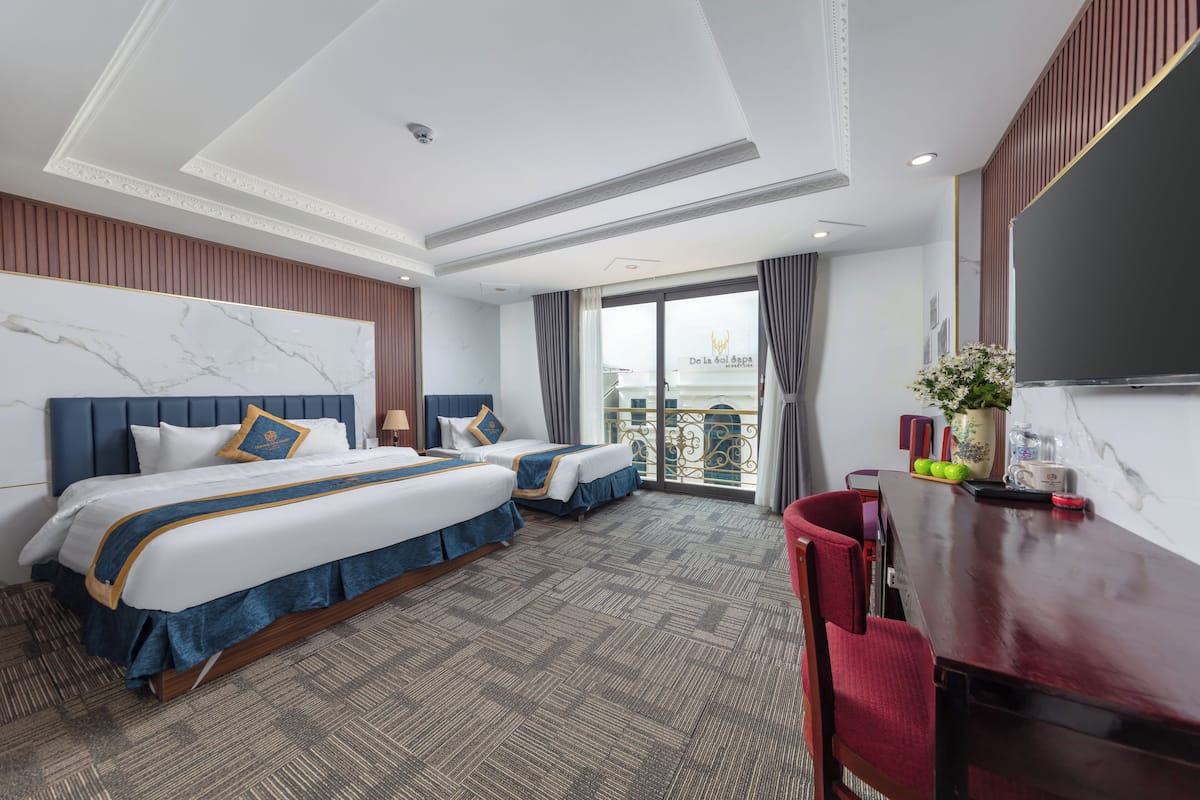 Quarto de hotel com duas camas, uma escrivaninha e uma varanda.