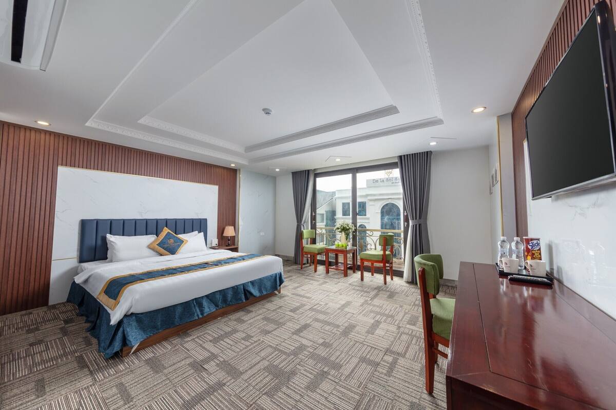 Quarto de hotel com uma cama grande, uma escrivaninha, uma cadeira, uma televisão e varanda com vista.