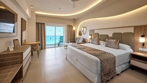 Quarto de hotel moderno com uma cama grande, uma escrivaninha, uma cadeira, televisão e varanda com vista para o mar.