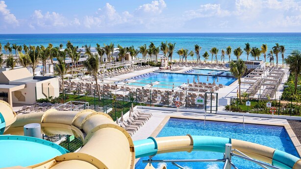 Um resort com várias piscinas, palmeiras e vista para o oceano.