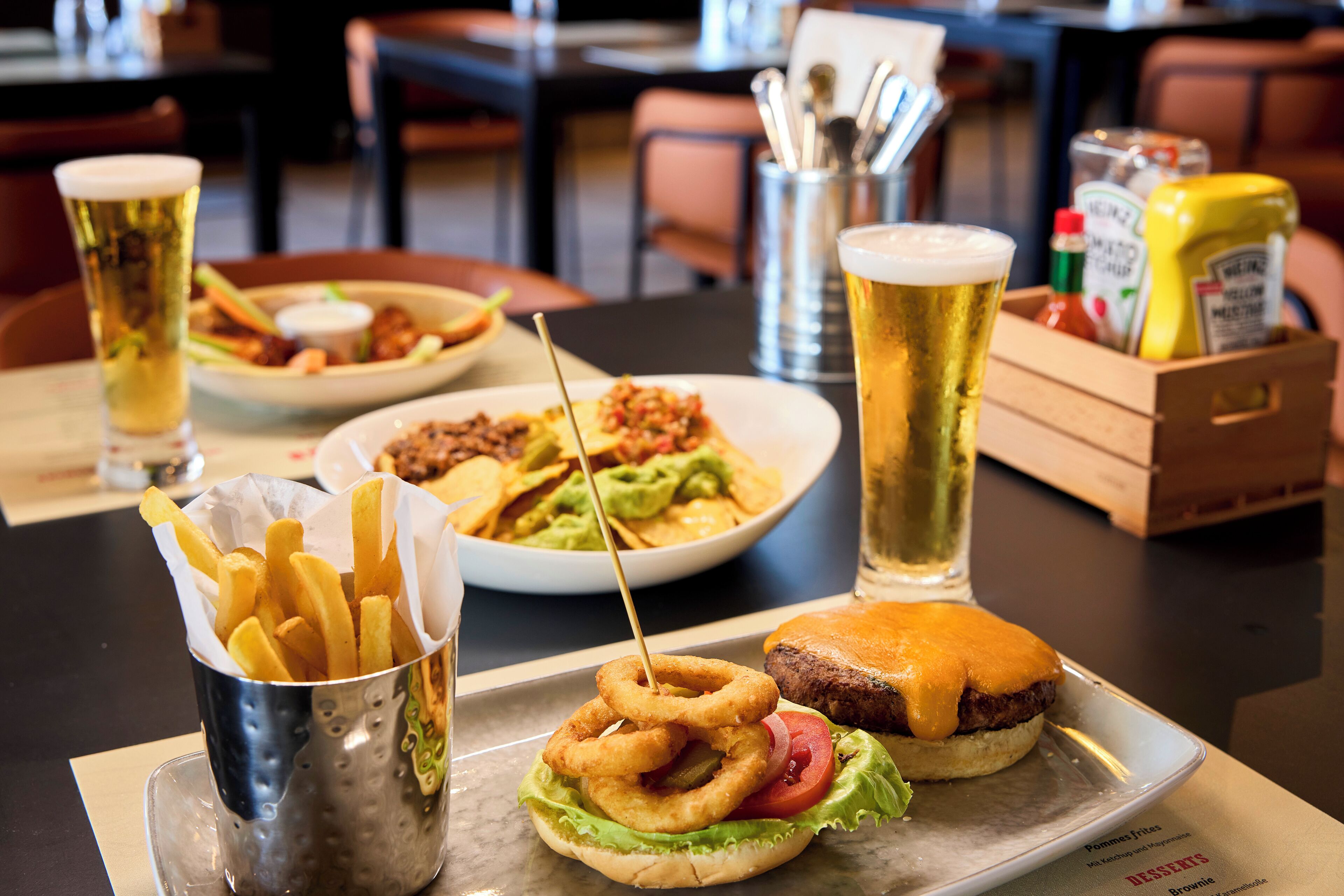 Uma mesa de jantar com um hambúrguer, anéis de cebola, batatas fritas e um copo de cerveja.