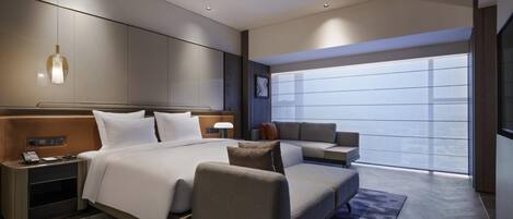 Quarto de hotel moderno com uma cama grande, um sofá, uma escrivaninha e uma janela ampla.