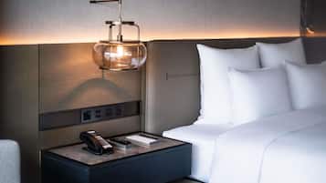 Quarto de hotel moderno com uma cama, mesa de cabeceira com telefone e controles remotos, e luminária pendente única.
