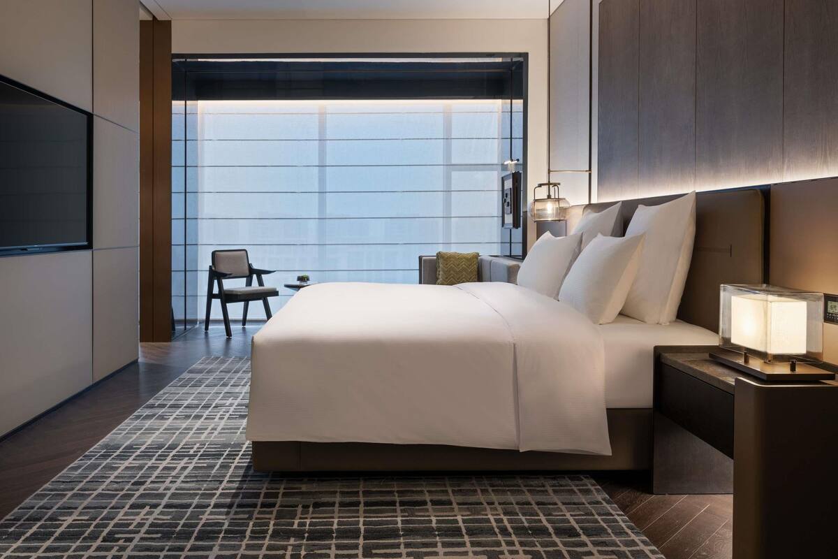 Quarto de hotel moderno com uma cama grande, televisão, escrivaninha e uma cadeira.