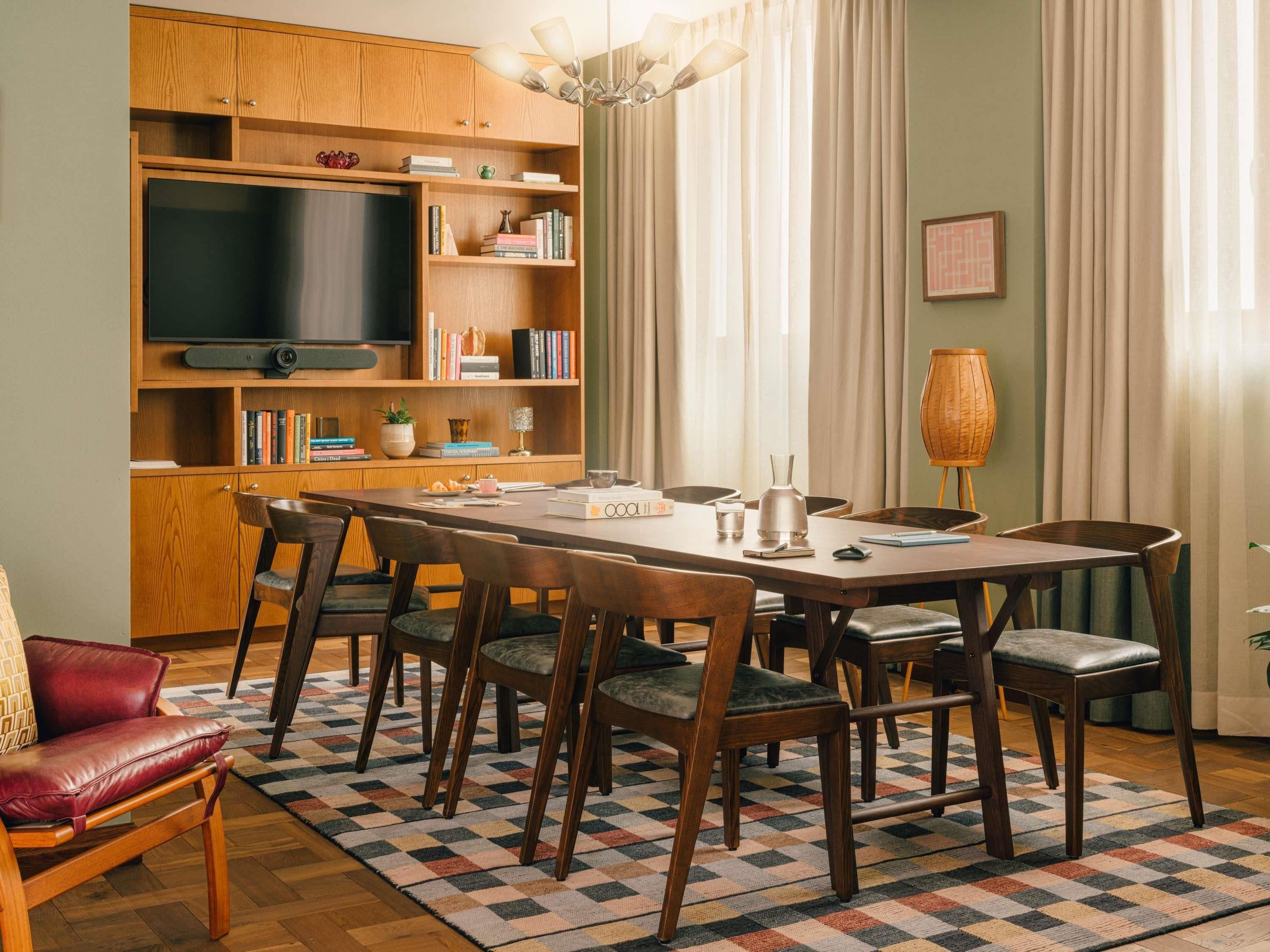 Uma sala de jantar com uma mesa de madeira, cadeiras, uma estante de livros, uma televisão e um abajur.