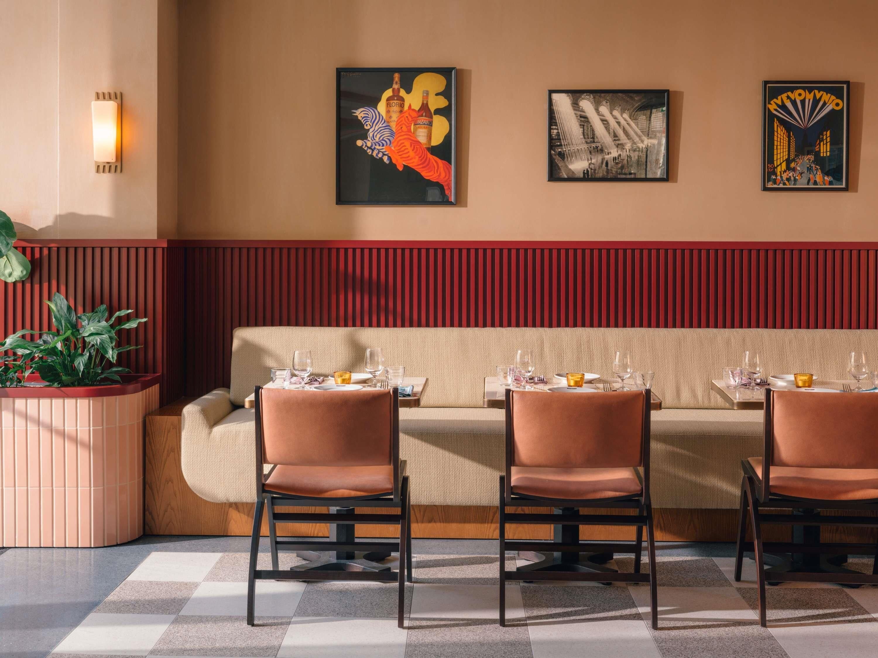 Interior de restaurante com sofá, mesas de jantar, obras de arte nas paredes e planta em vaso.