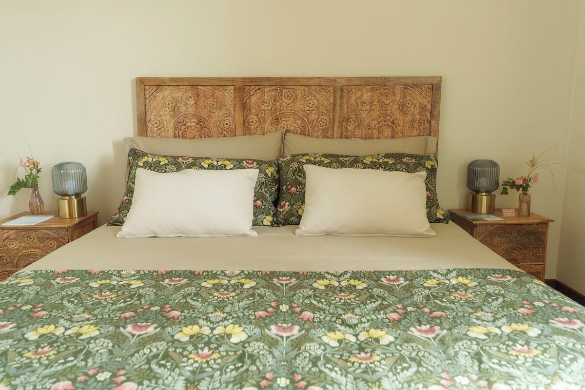 Uma cama com colcha florida, duas almofadas e cabeceira de madeira.